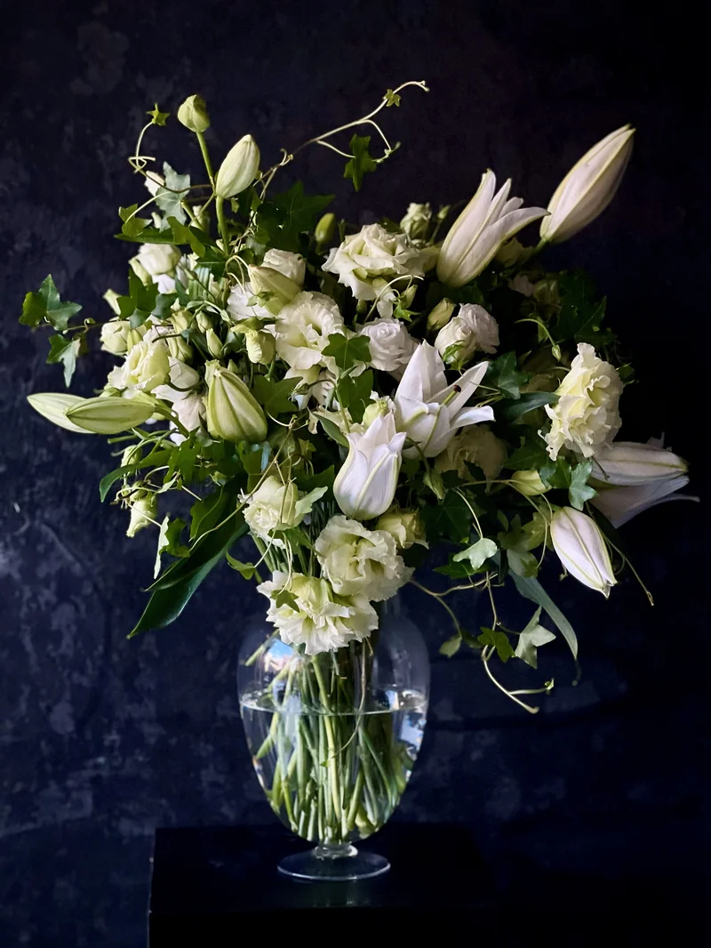 White lilies and green lisianthus with ivy in a clear vase.
